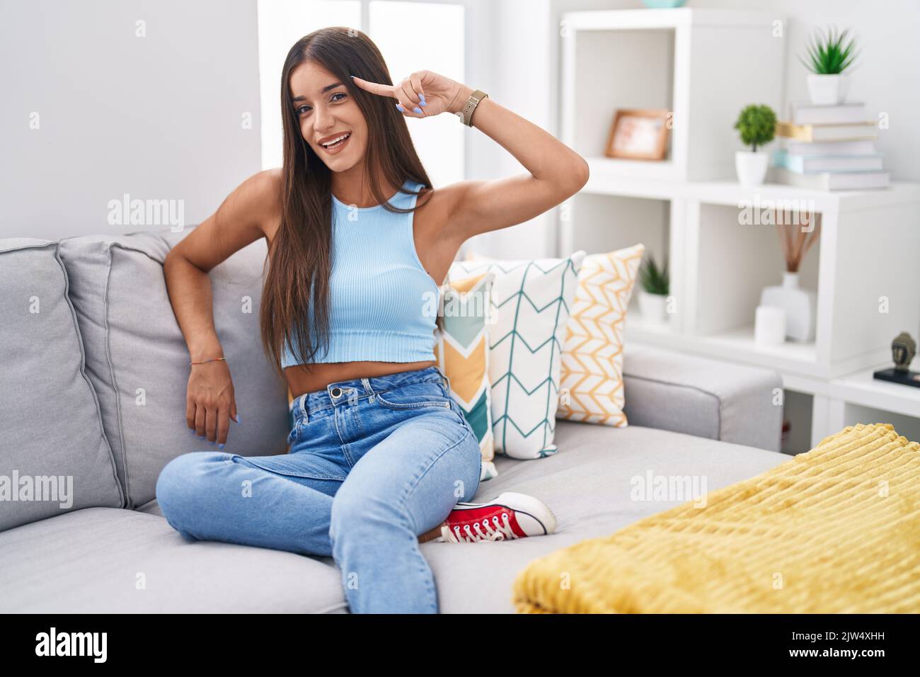 Young brunette woman sitting on the sofa at home smiling pointing to ...