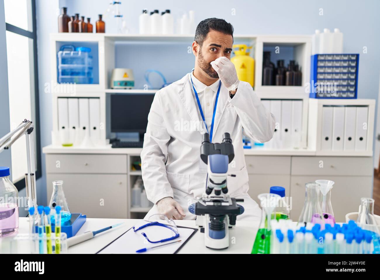 Young hispanic man with beard working at scientist laboratory smelling ...