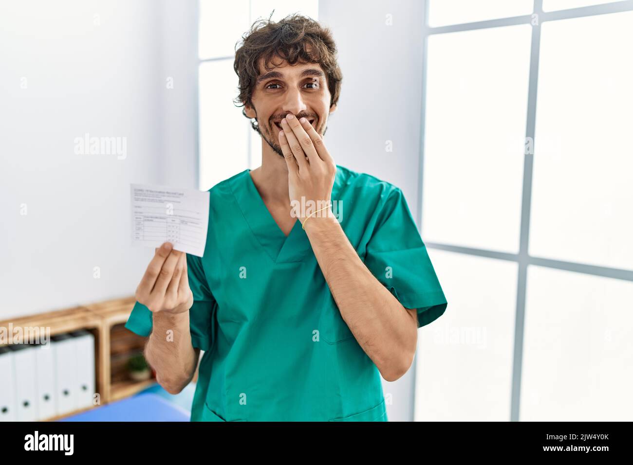 Young hispanic doctor man holding covid record card laughing and ...