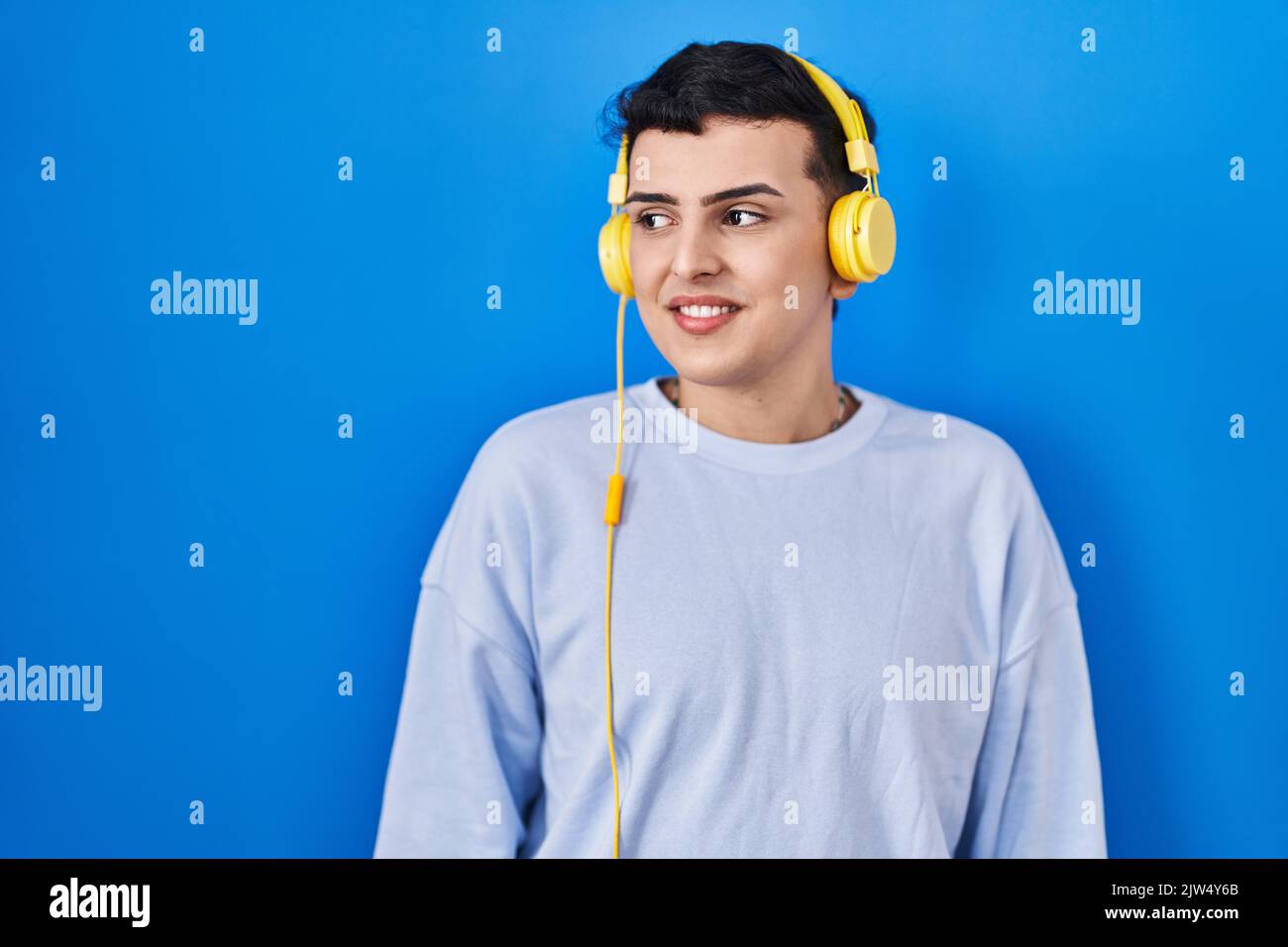 Non binary person listening to music using headphones looking away to ...