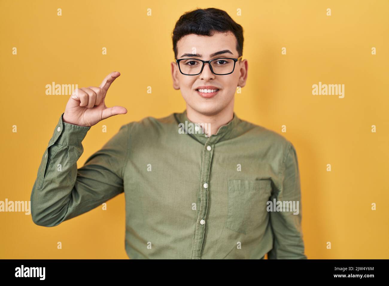 Non binary person standing over yellow background smiling and confident ...
