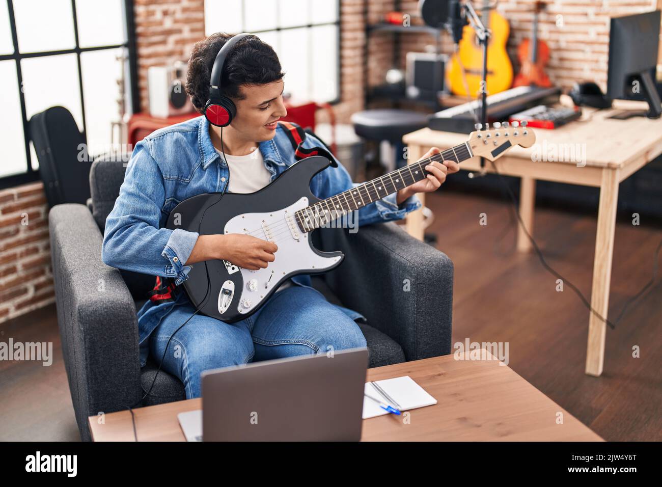Young non binary man musician having online electric guitar lesson at ...
