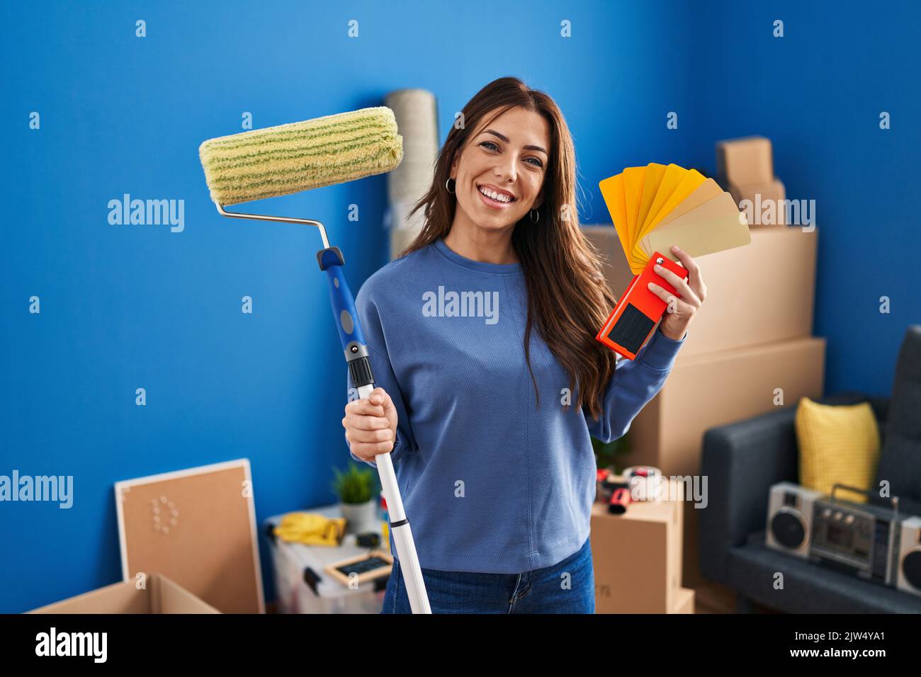 Young brunette woman holding roller painter painting new house smiling ...