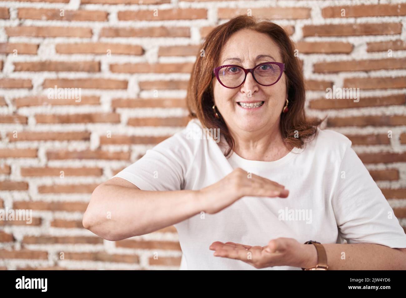 Senior woman with glasses standing over bricks wall gesturing with ...