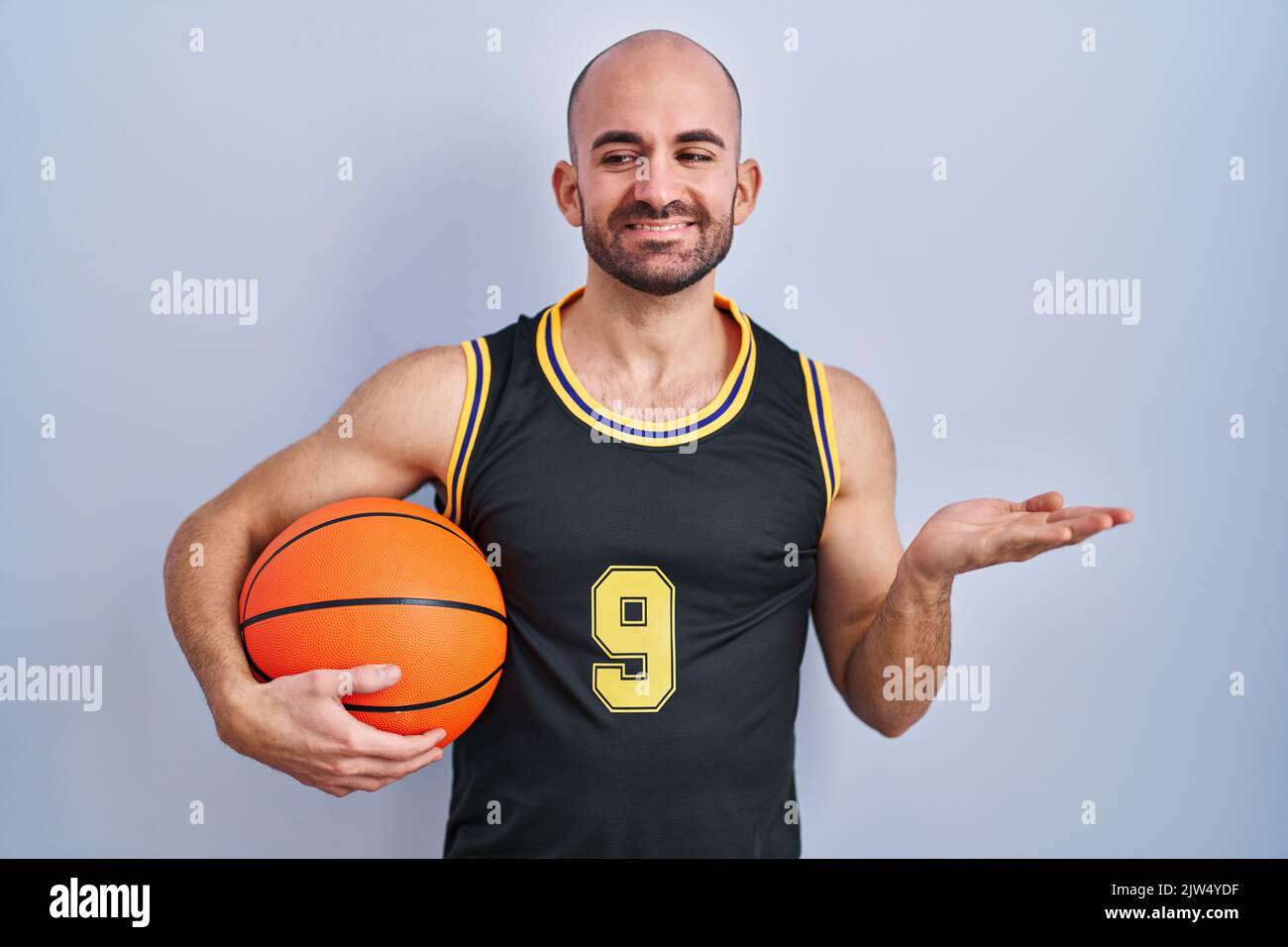 Young bald man with beard wearing basketball uniform holding ball ...