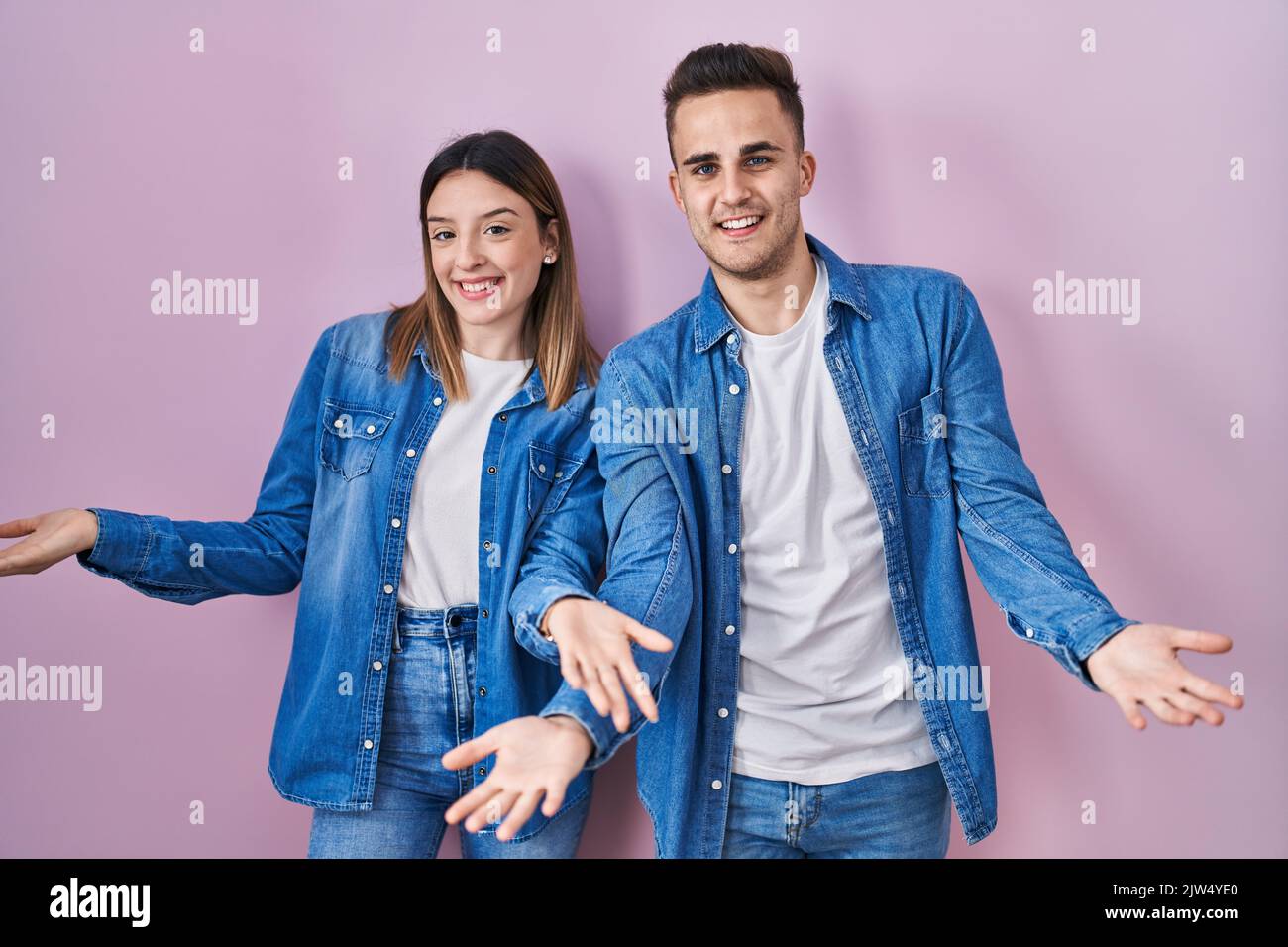 Young hispanic couple standing over pink background smiling cheerful ...