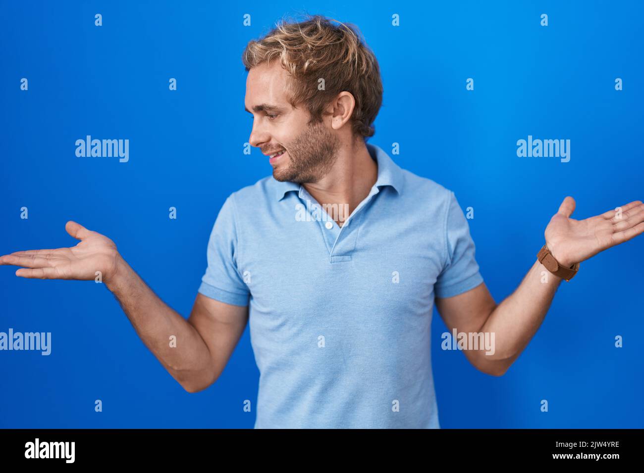 Caucasian man standing over blue background smiling showing both hands ...