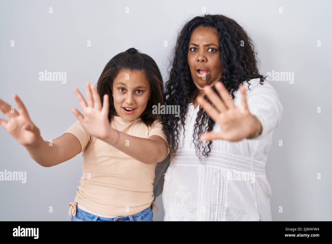 Mother and young daughter standing over white background afraid and ...