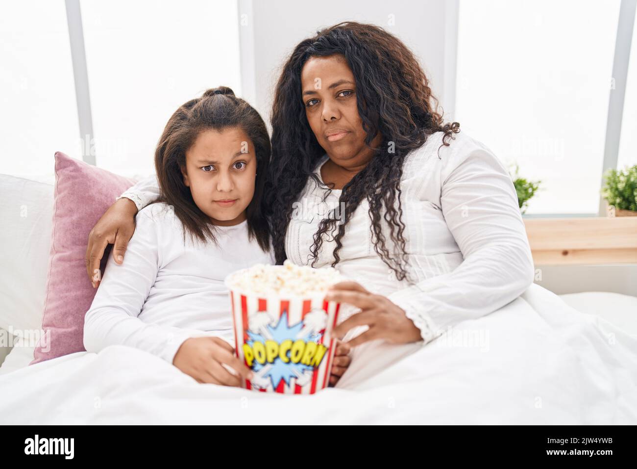 Mother and young daughter eating popcorn in the bed skeptic and nervous ...