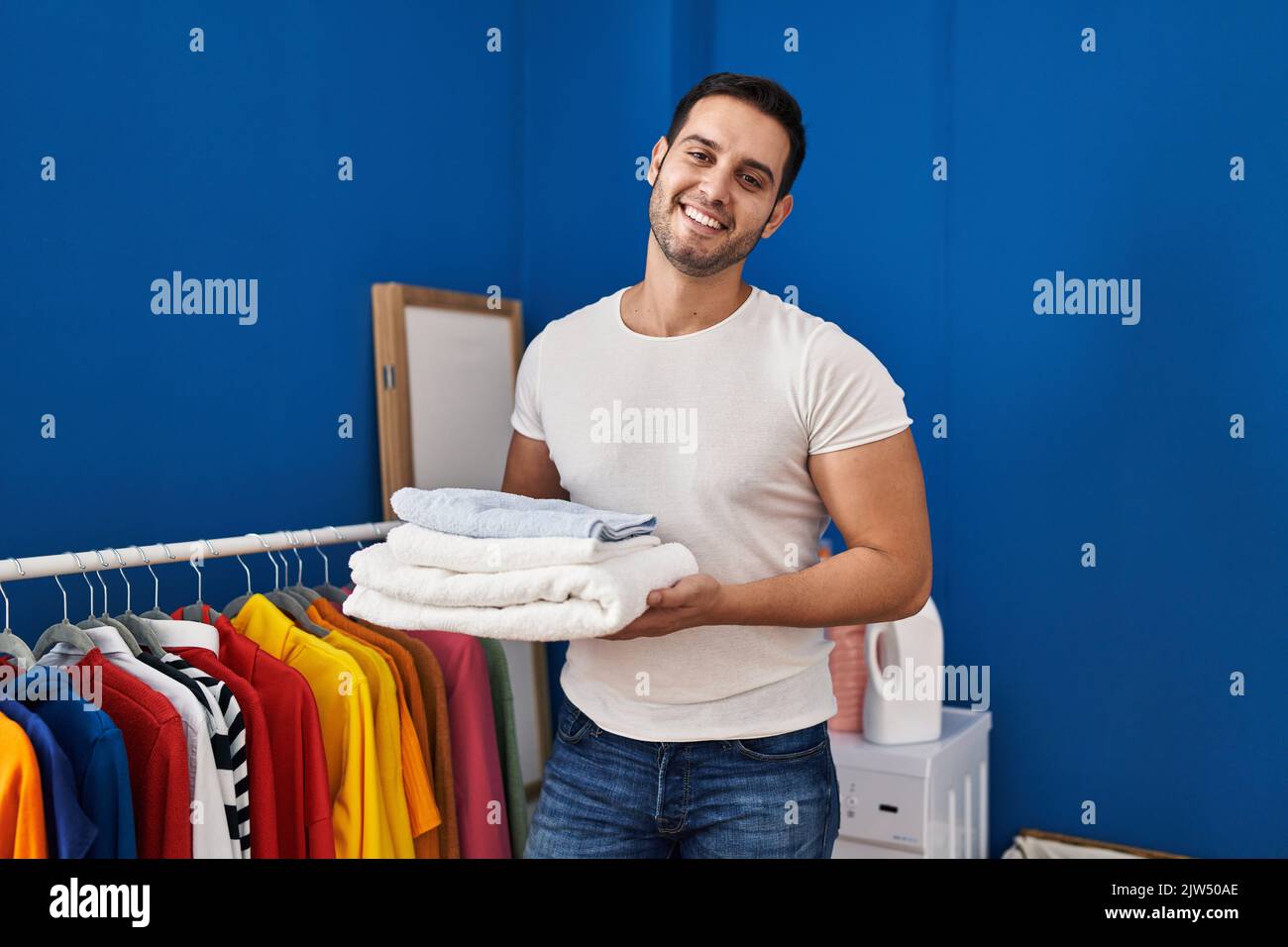 Young hispanic man with beard holding folded clean towels at laundry ...
