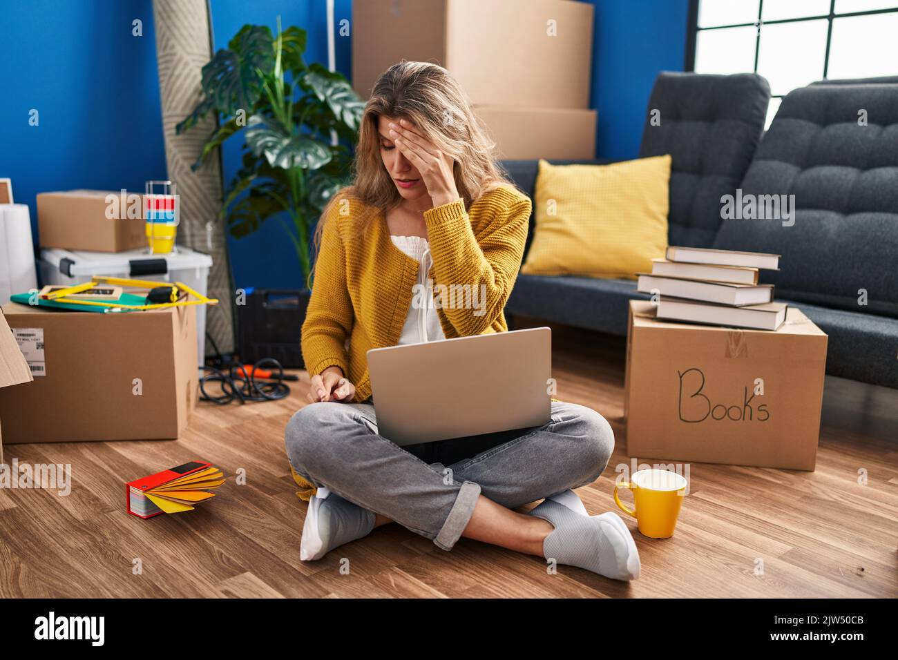 Young woman sitting on the floor at new home using laptop with sad ...