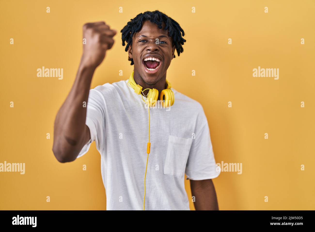 Young african man with dreadlocks standing over yellow background angry ...