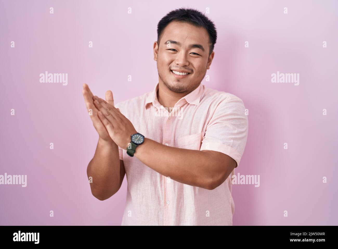 Chinese young man standing over pink background clapping and applauding ...