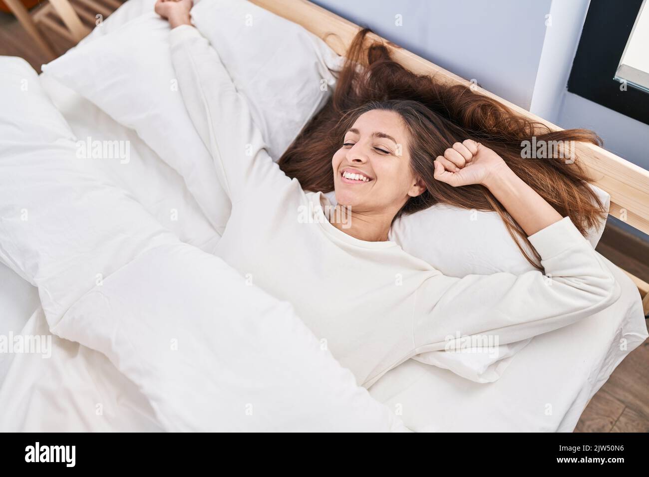 Young woman stretching arms lying on bed at bedroom Stock Photo - Alamy