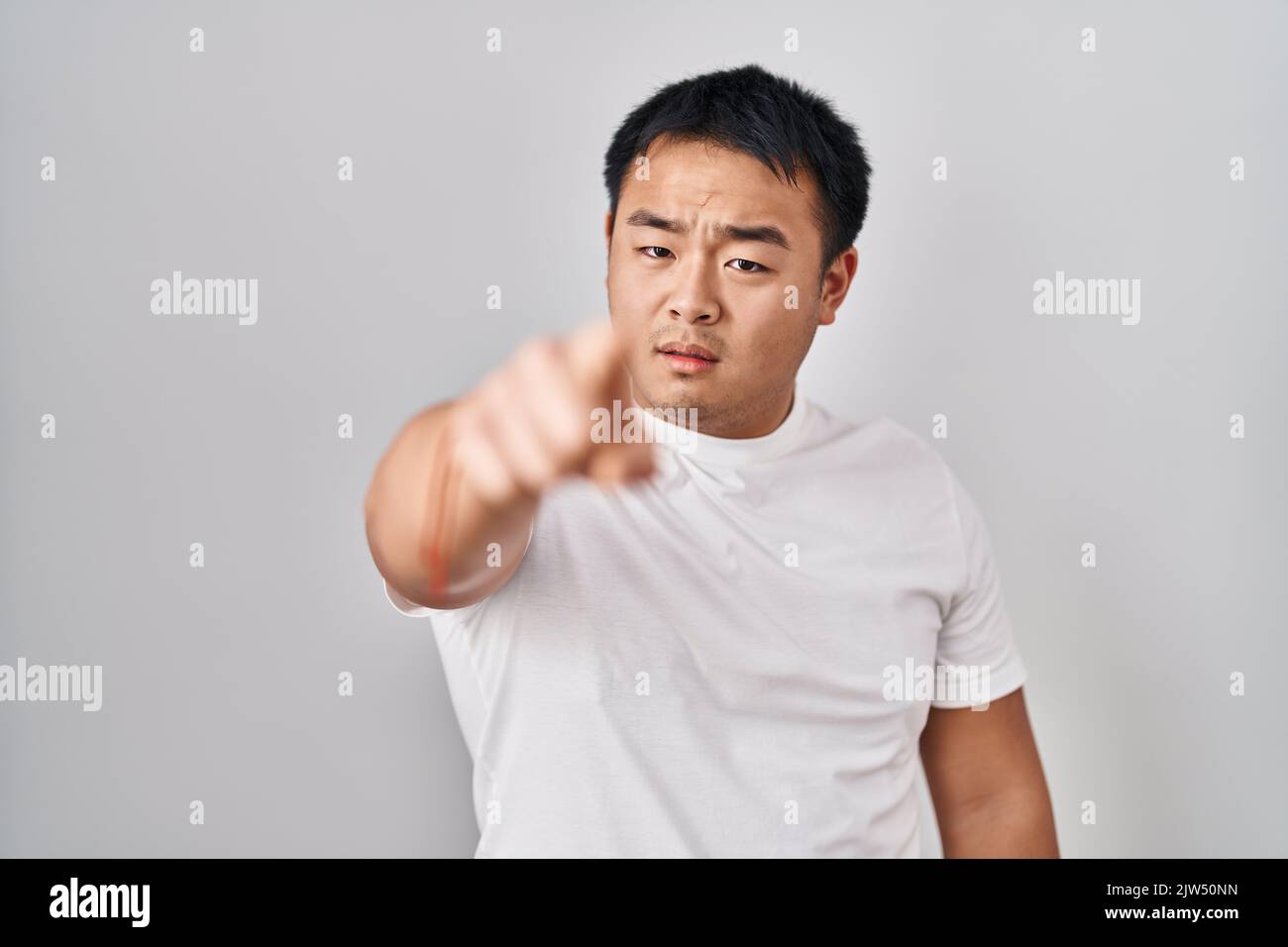 Young chinese man standing over white background pointing displeased ...