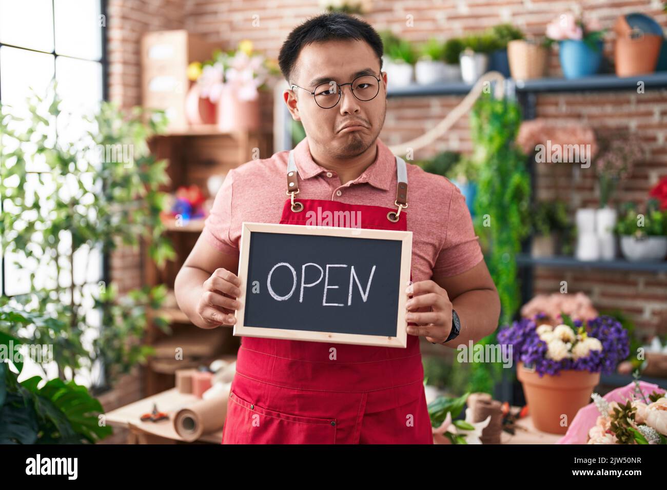 Chinese young man working at florist holding open sign depressed and ...