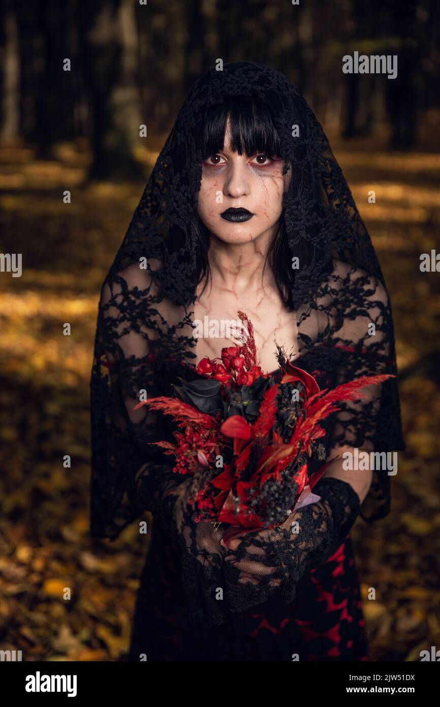 A Pretty gothic caucasian female in a black dress posing in the park ...