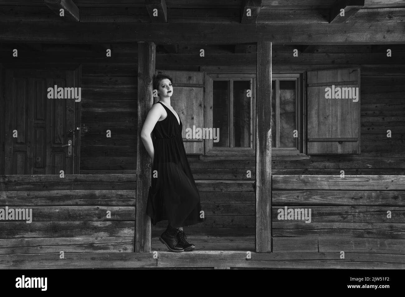 A grayscale of a Caucasian lady standing and posing next to wooden ...