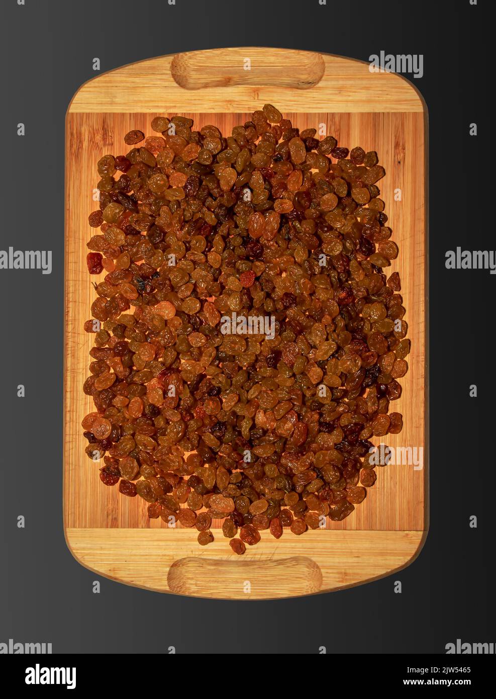 Raisins on a wooden board for the background. Isolated over black ...