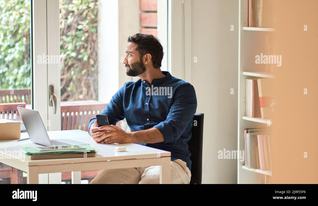Indian professional business man holding smartphone working at home ...