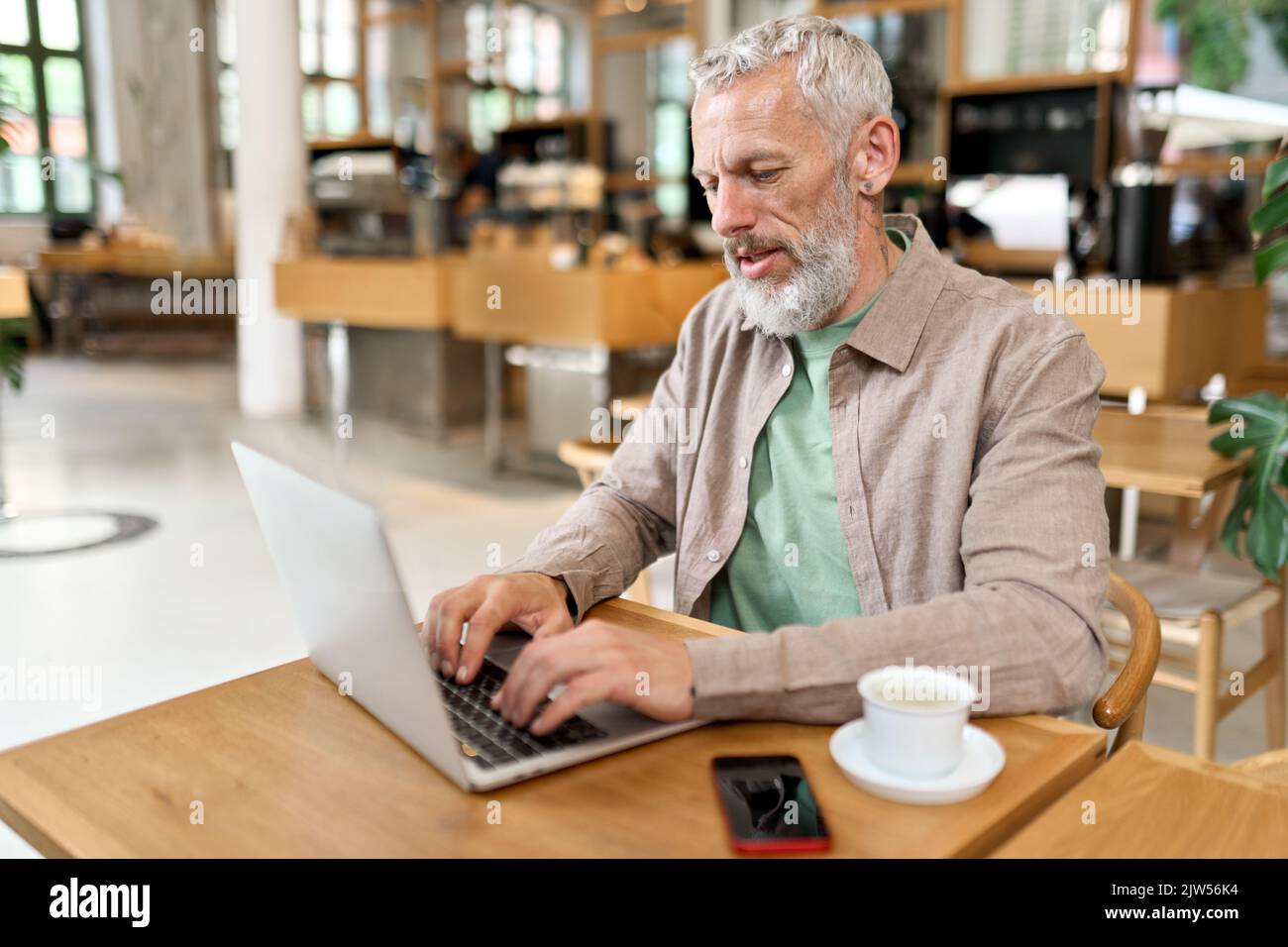 Busy mature professional man using laptop sitting in cafe working ...