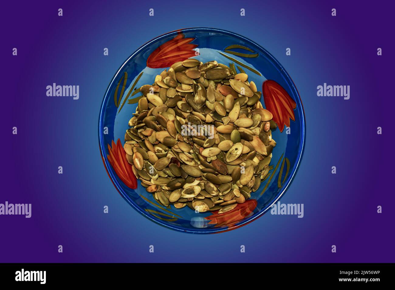 Peeled roasted pumpkin seeds in a glass blue bowl. Isolated macro photo ...