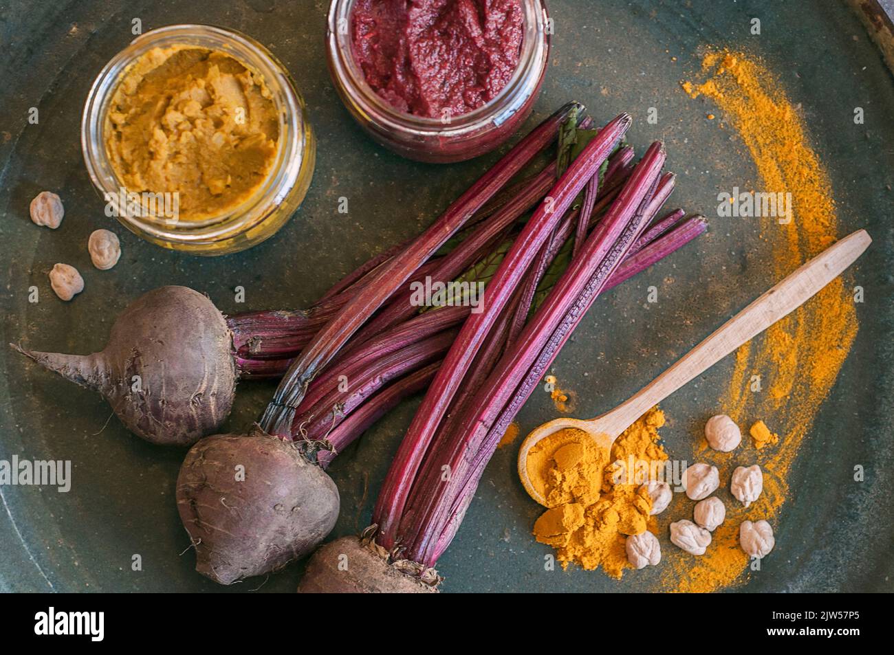 Turmeric and beet dip inside a jar and all the ingredients on a blue ...