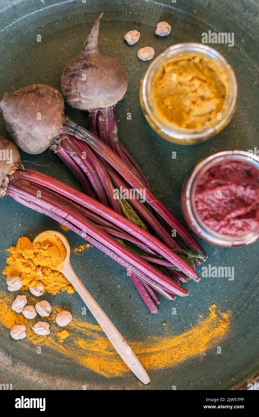 Turmeric and beet dip inside a jar and all the ingredients on a blue ...