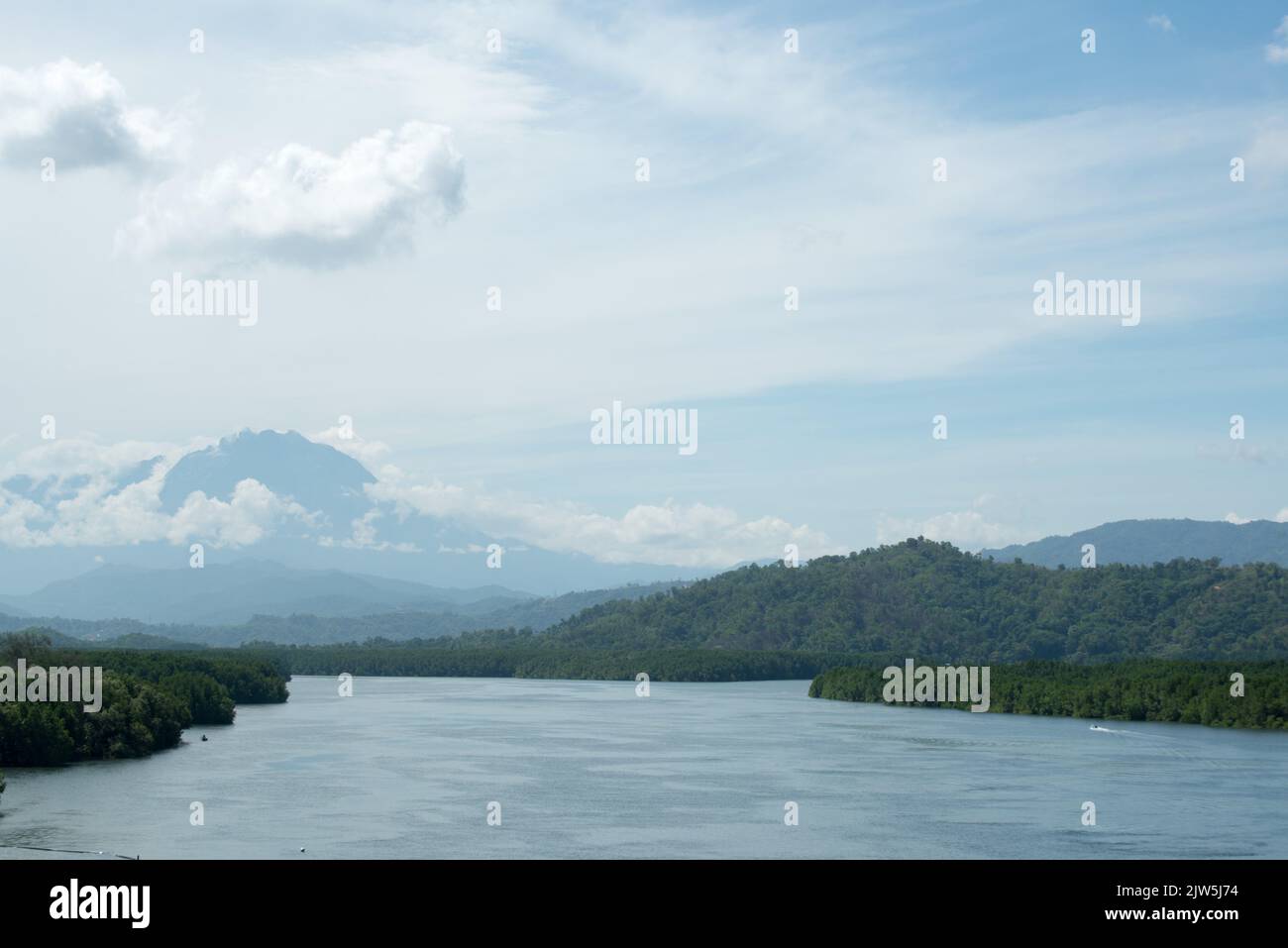 A river with greenery around and cloudy mountains in the background ...