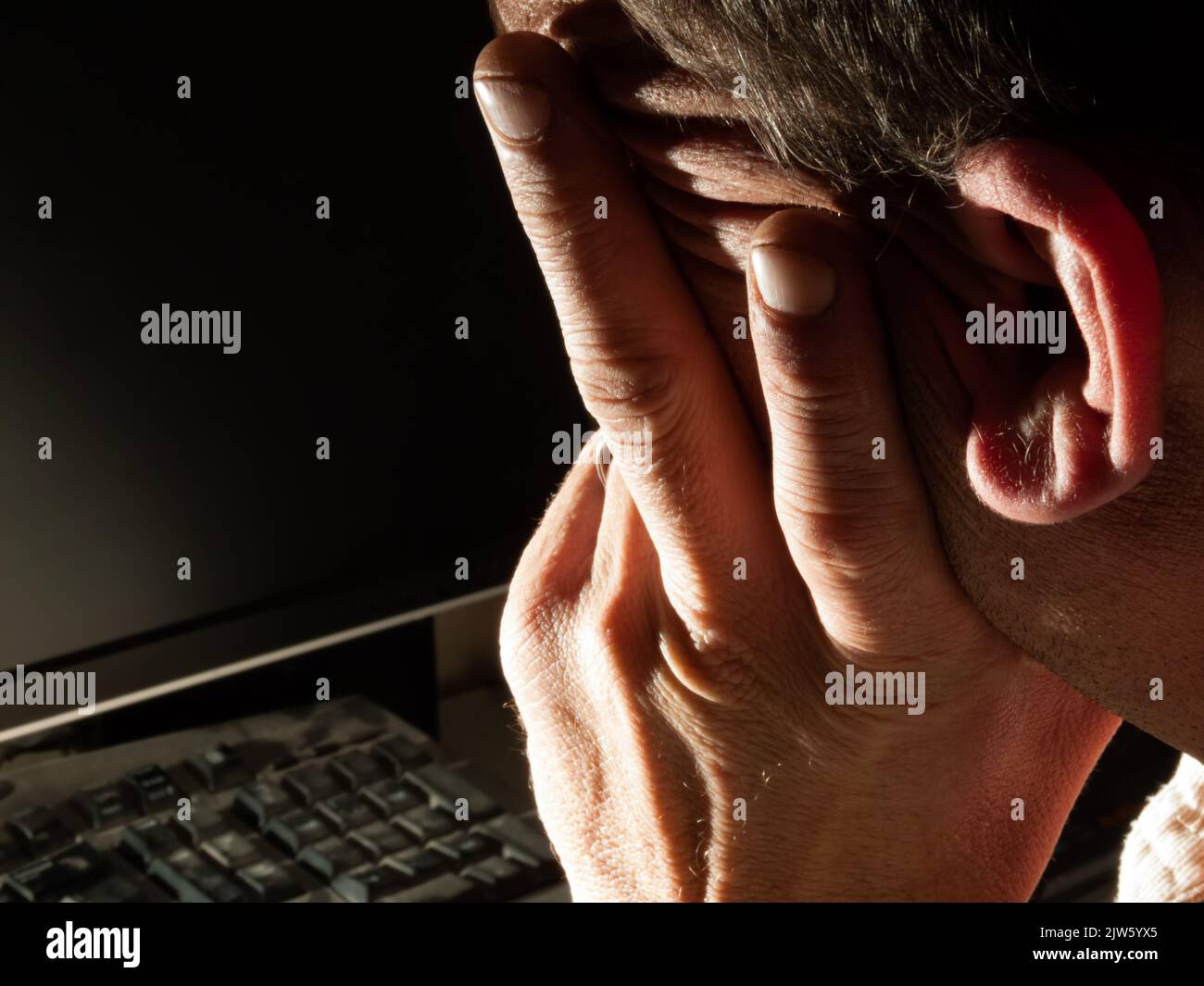 Man resting his head on his hand staring at a broken computer with a ...