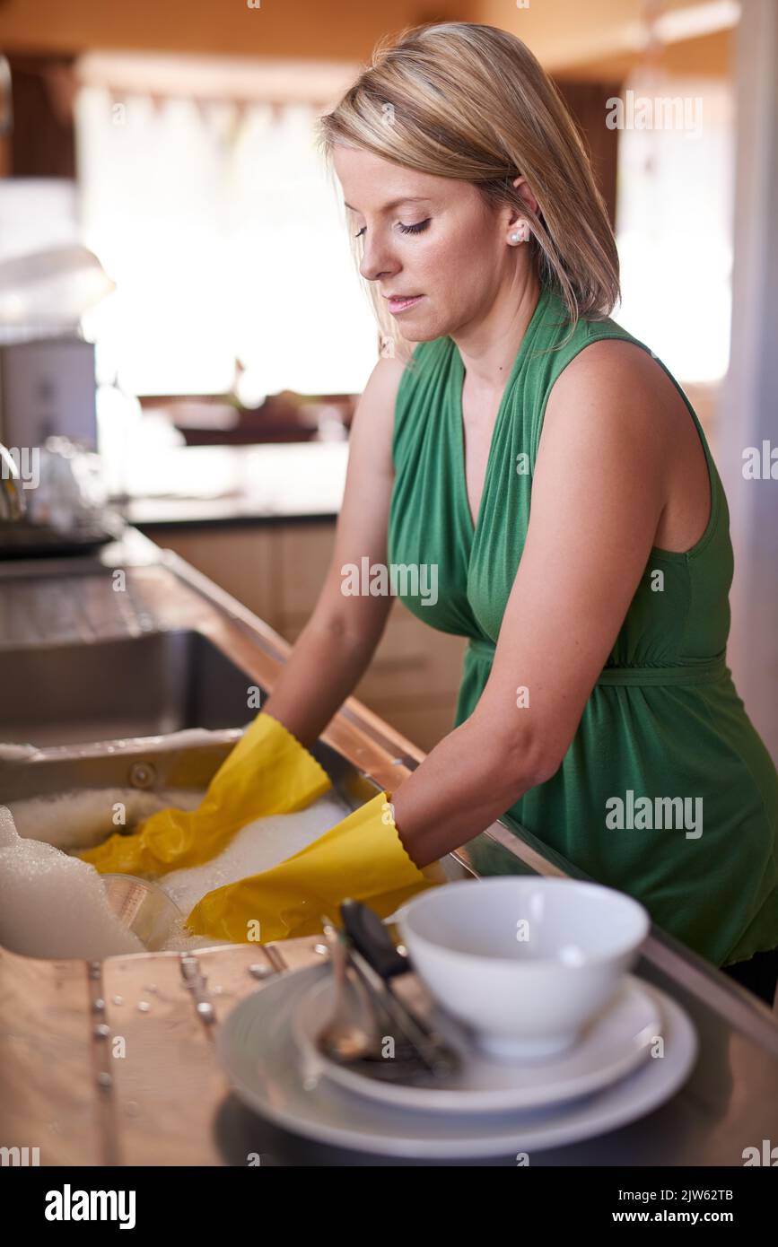 Tackling some housework. a young woman washing dishes in a kitchen ...
