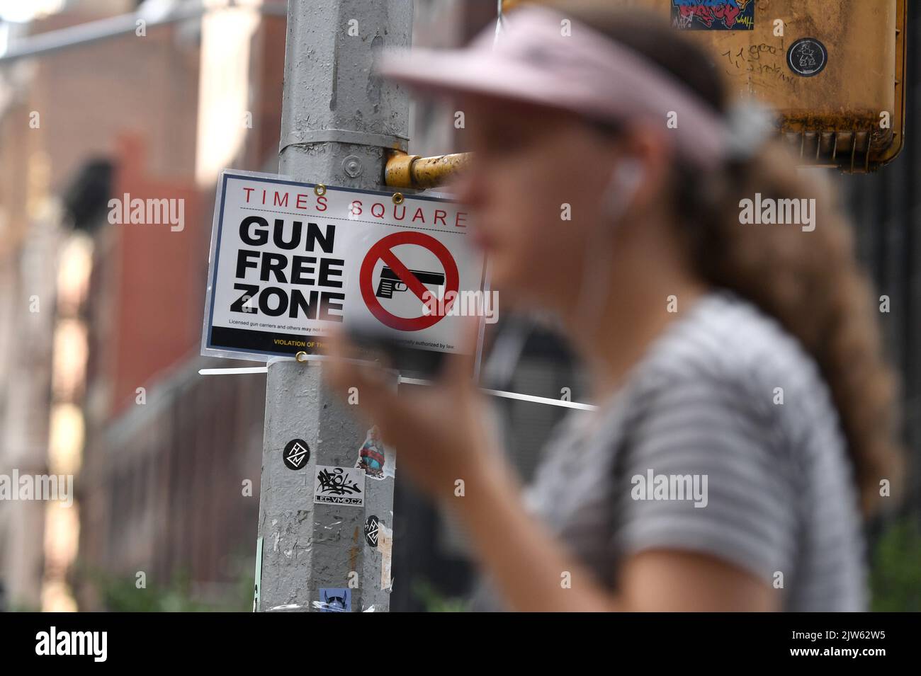 A woman walks past a “Gun Free Zone” sign attached to a traffic light ...