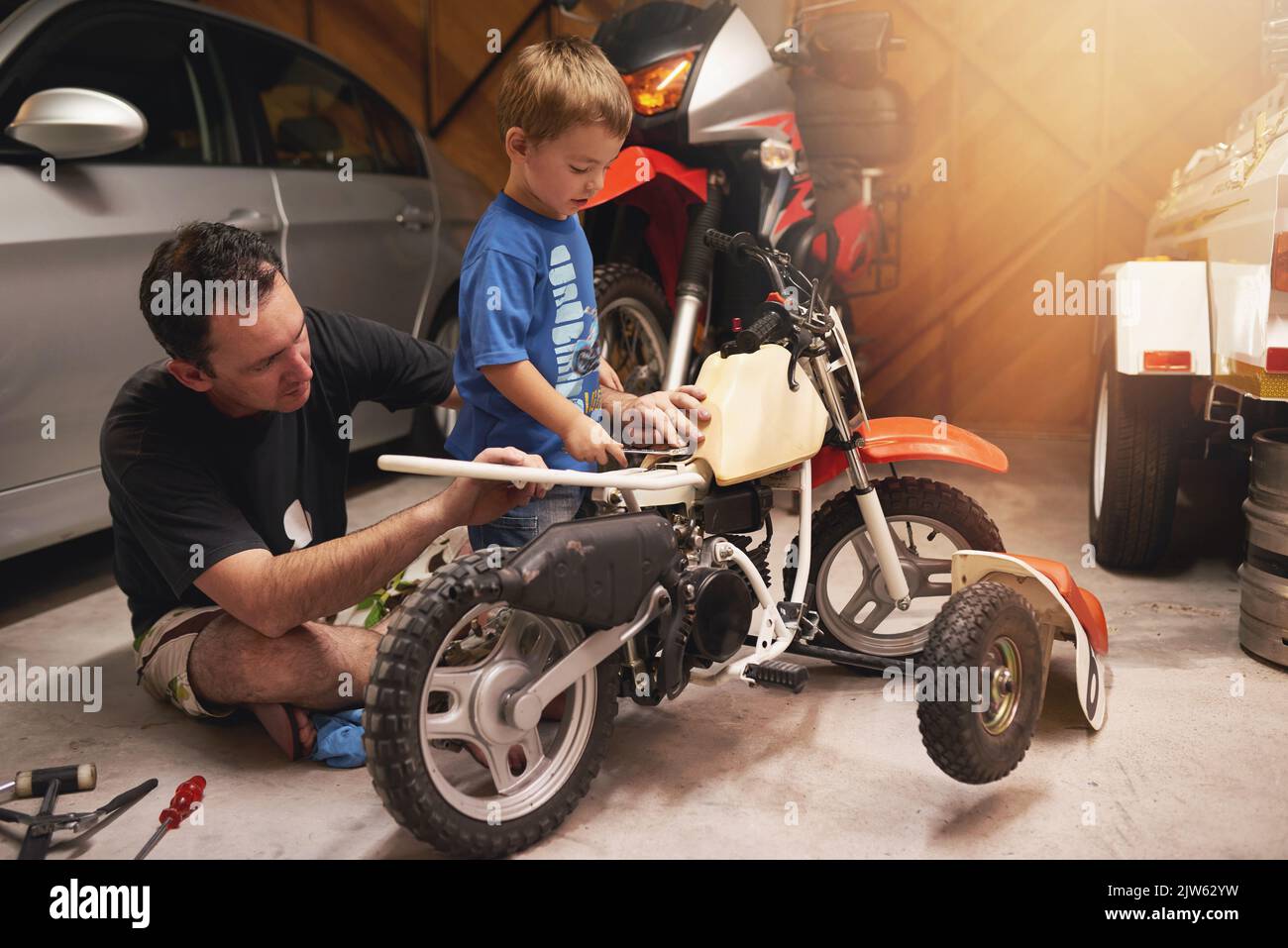 Hes learning lots from dad. a father and son fixing a bike in a garage ...