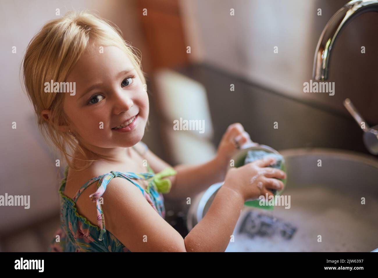 Keeping things clean. Portrait of a little girl washing dishes at home ...