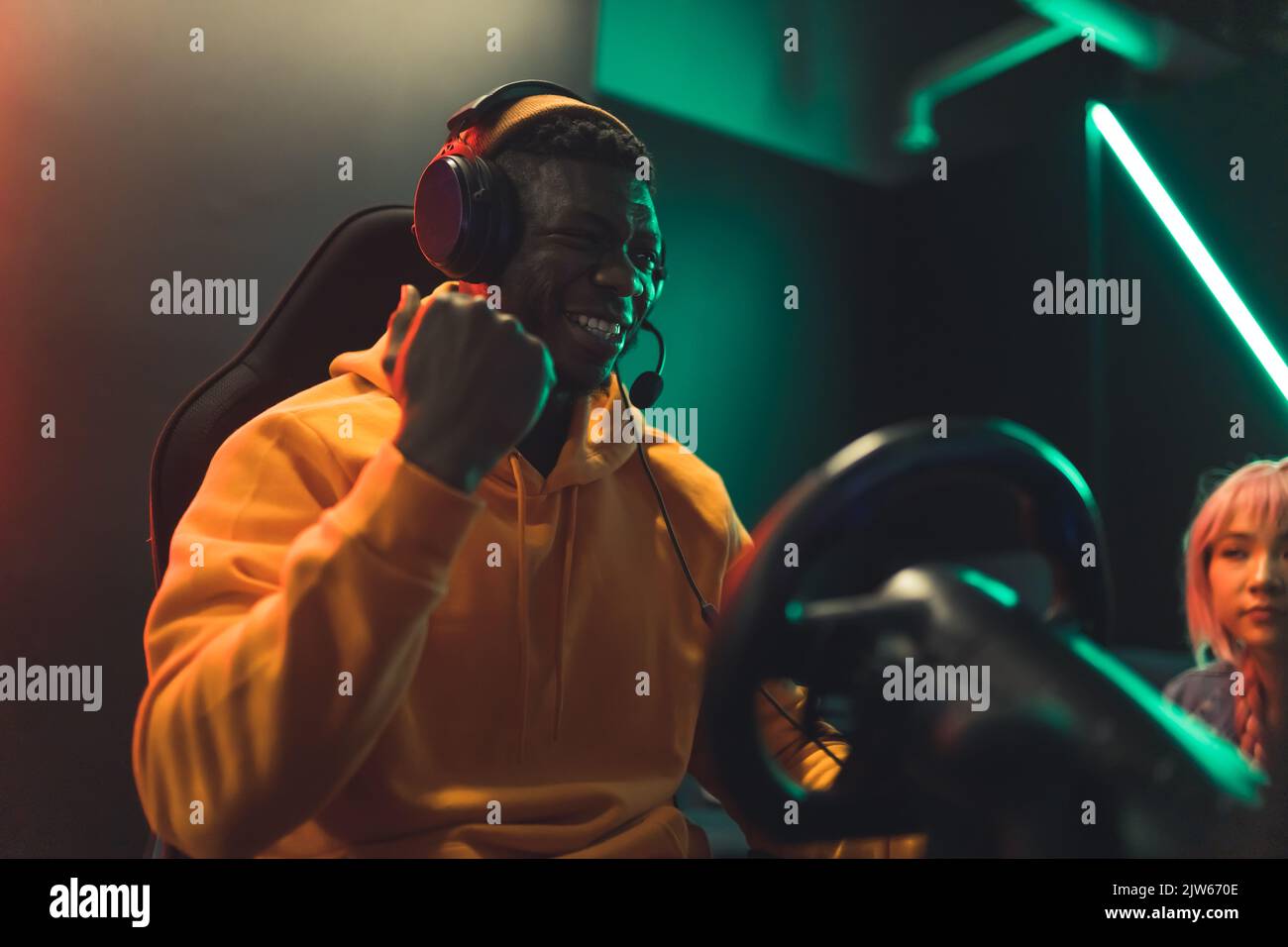 Teenage black guy wearing headset and orange hoodie celebrating victory ...