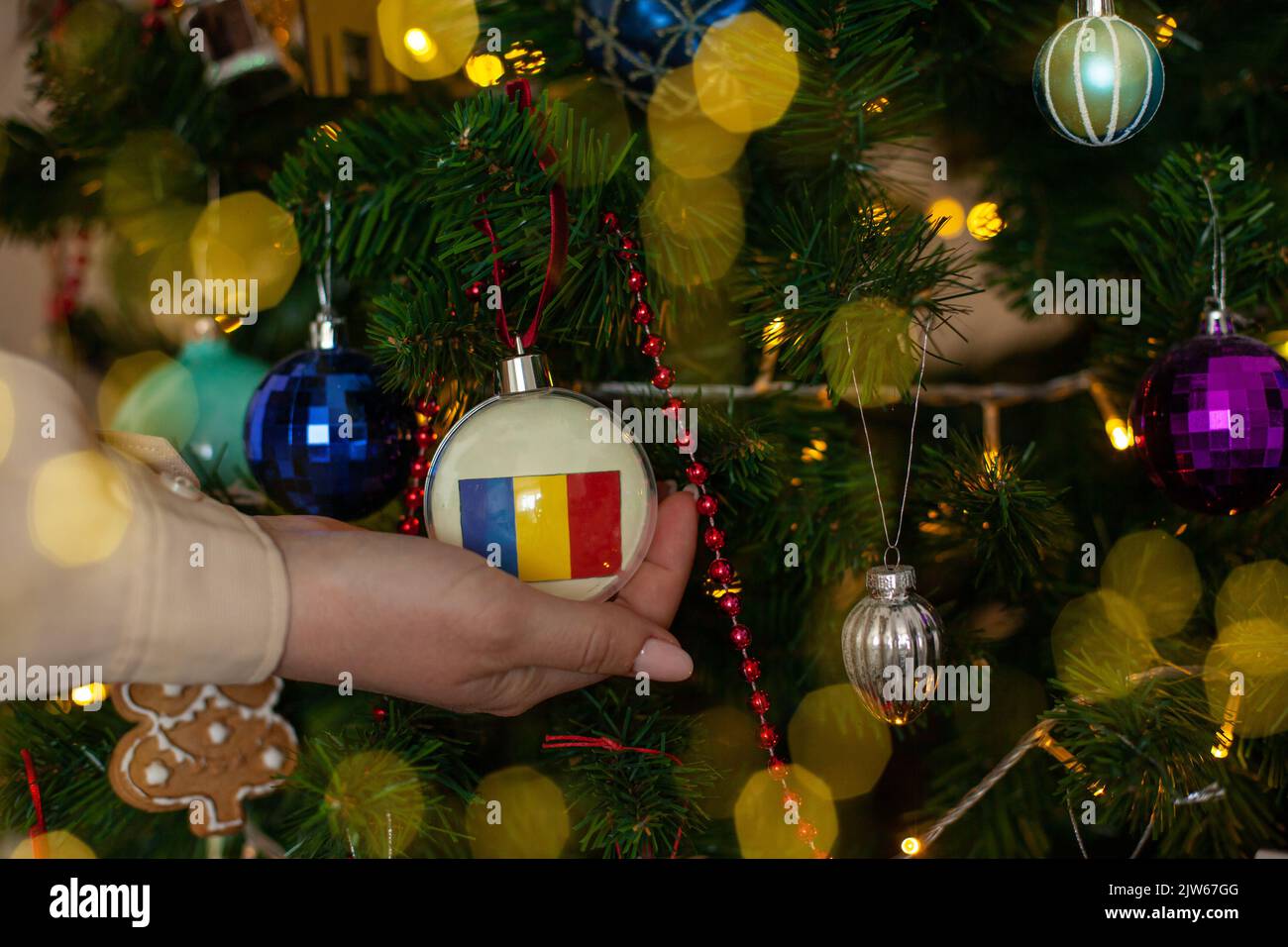 a girl holds a decoration on a Christmas tree with the flag of Romania ...