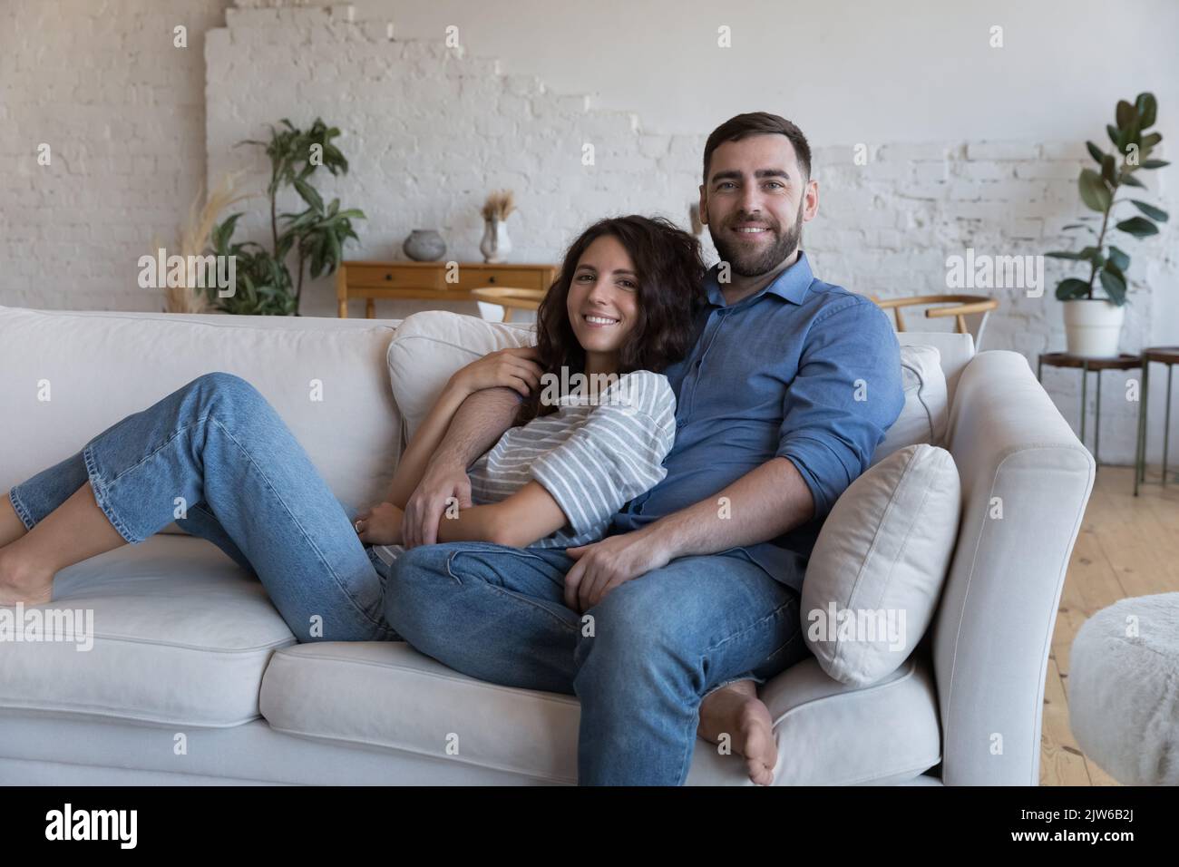 Multi-ethnic couple relaxing on comfortable couch smile pose for camera ...