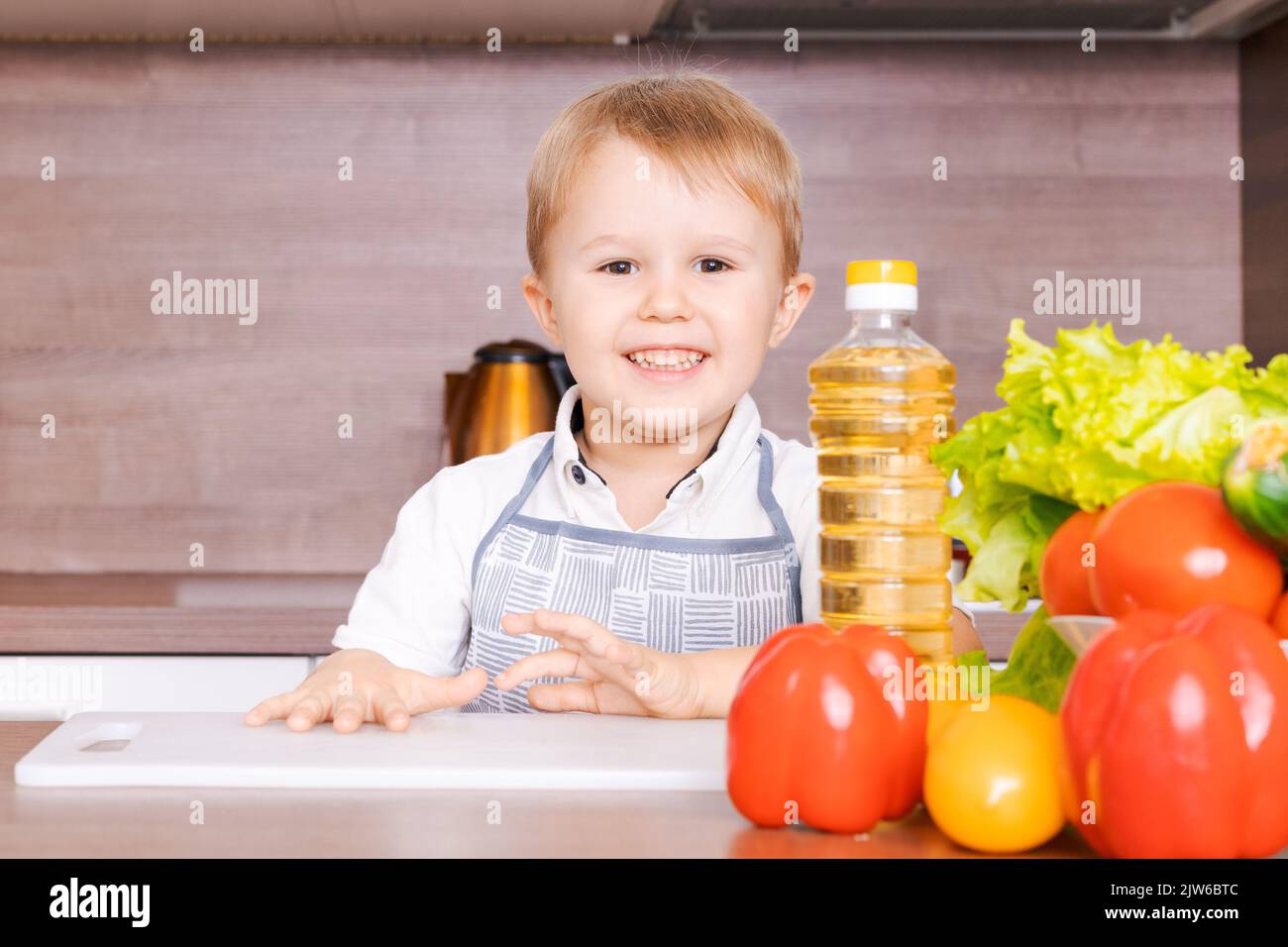 Little boy cook and an apron in kitchen smiles, vegetables and ...