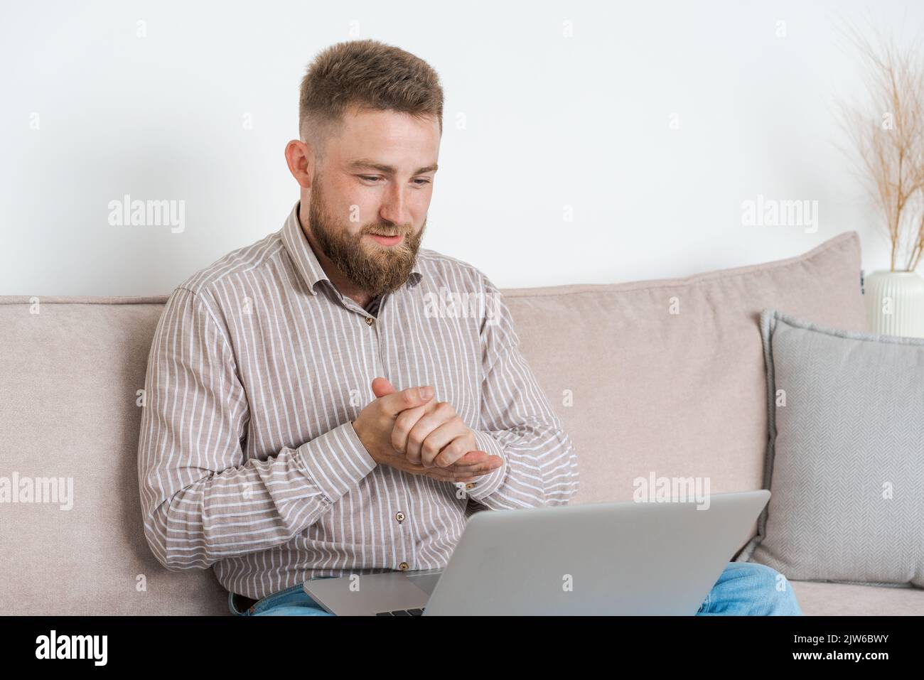 Young bearded man smiles while reading laptop screen while relaxing on ...