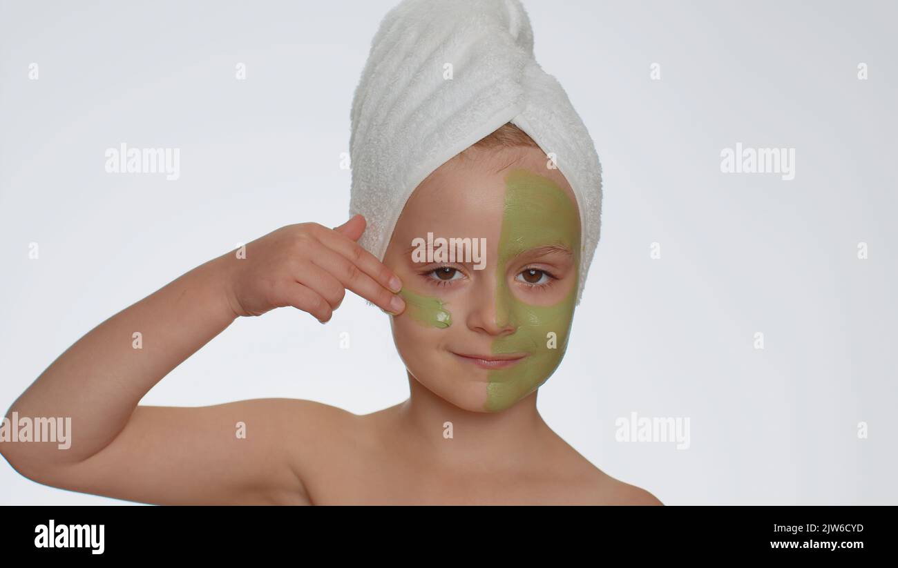 Beautiful young smiling child girl in towel on head applying cleansing ...