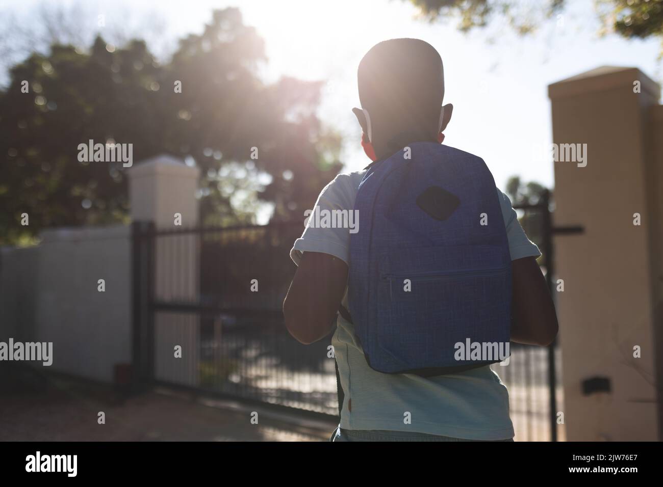 Rear view of african american boy wearing face mask with backpack ...
