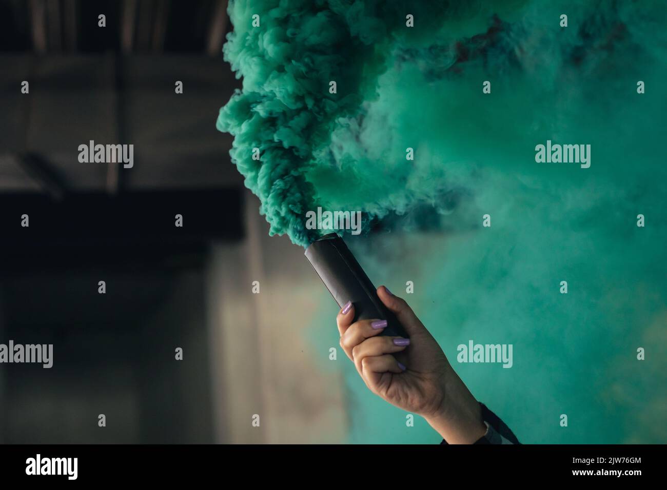 Hand of mixed race woman holding green smoke flare in empty room Stock ...