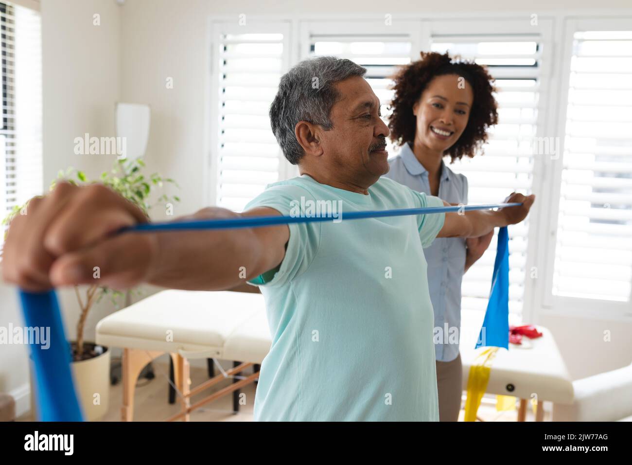 Mixed Race Female Physiotherapist Helping Senior Man Exercise Using