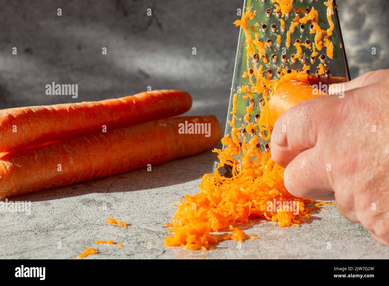 Grating a carrot on a stainless steel grater. On a concrete background ...