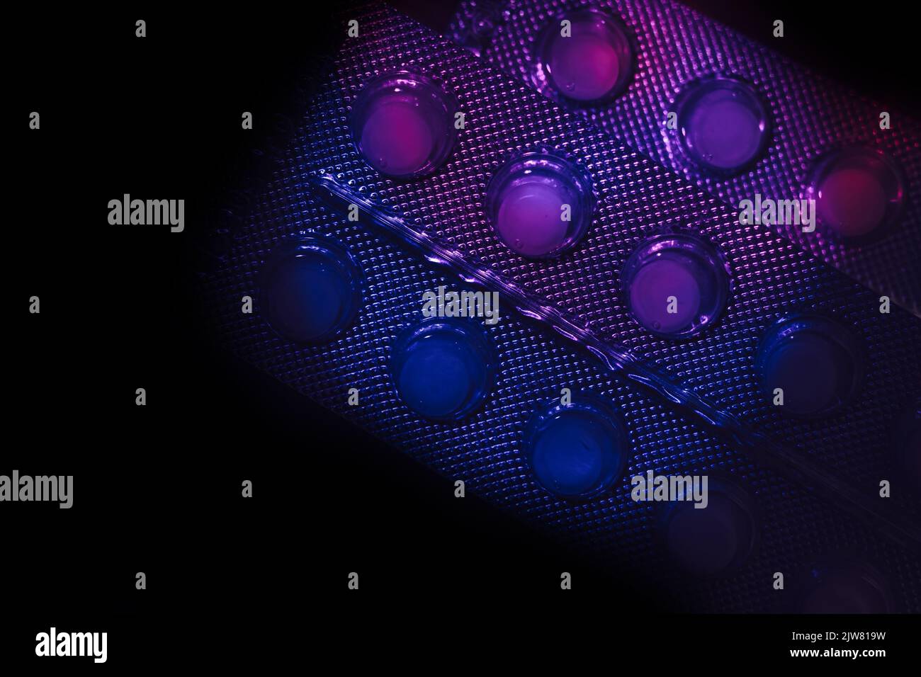 Pills or drugs in a package under neon light on a dark background ...
