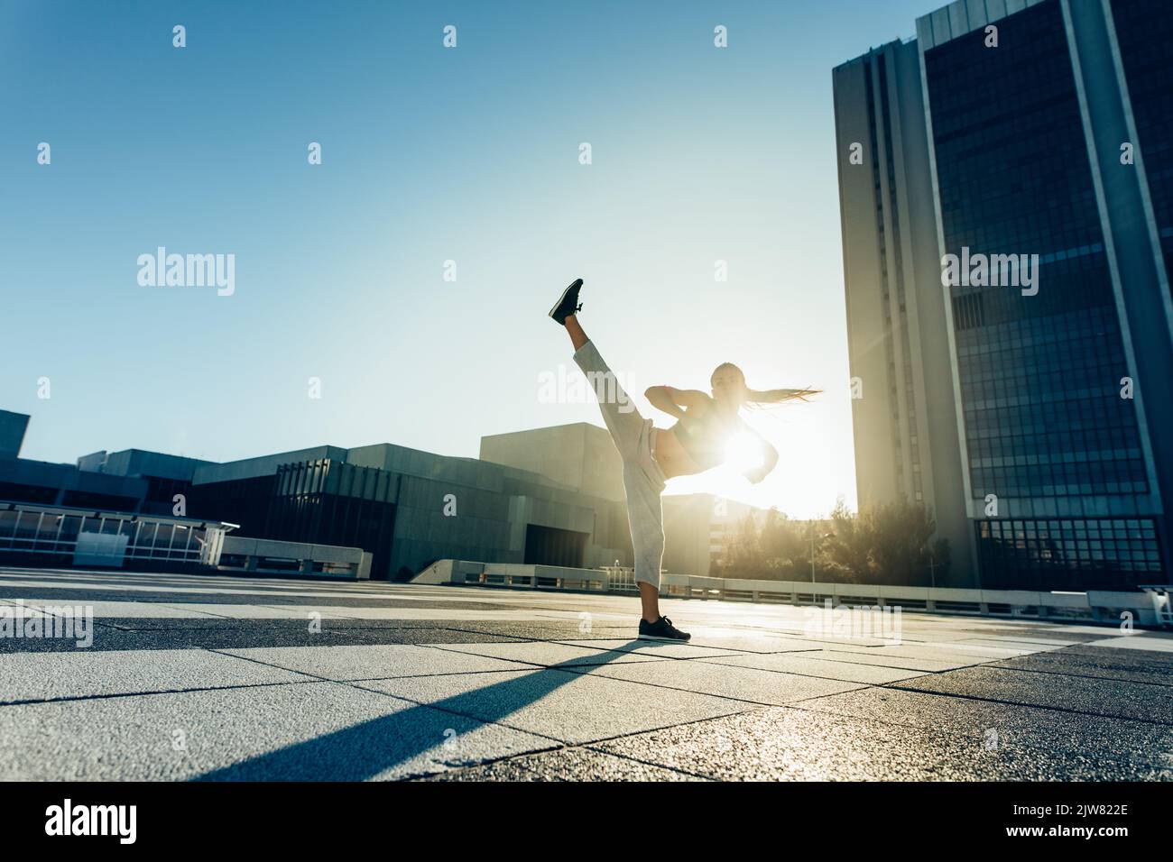 Urban woman doing high roundhouse kick outdoors in the city. Female ...