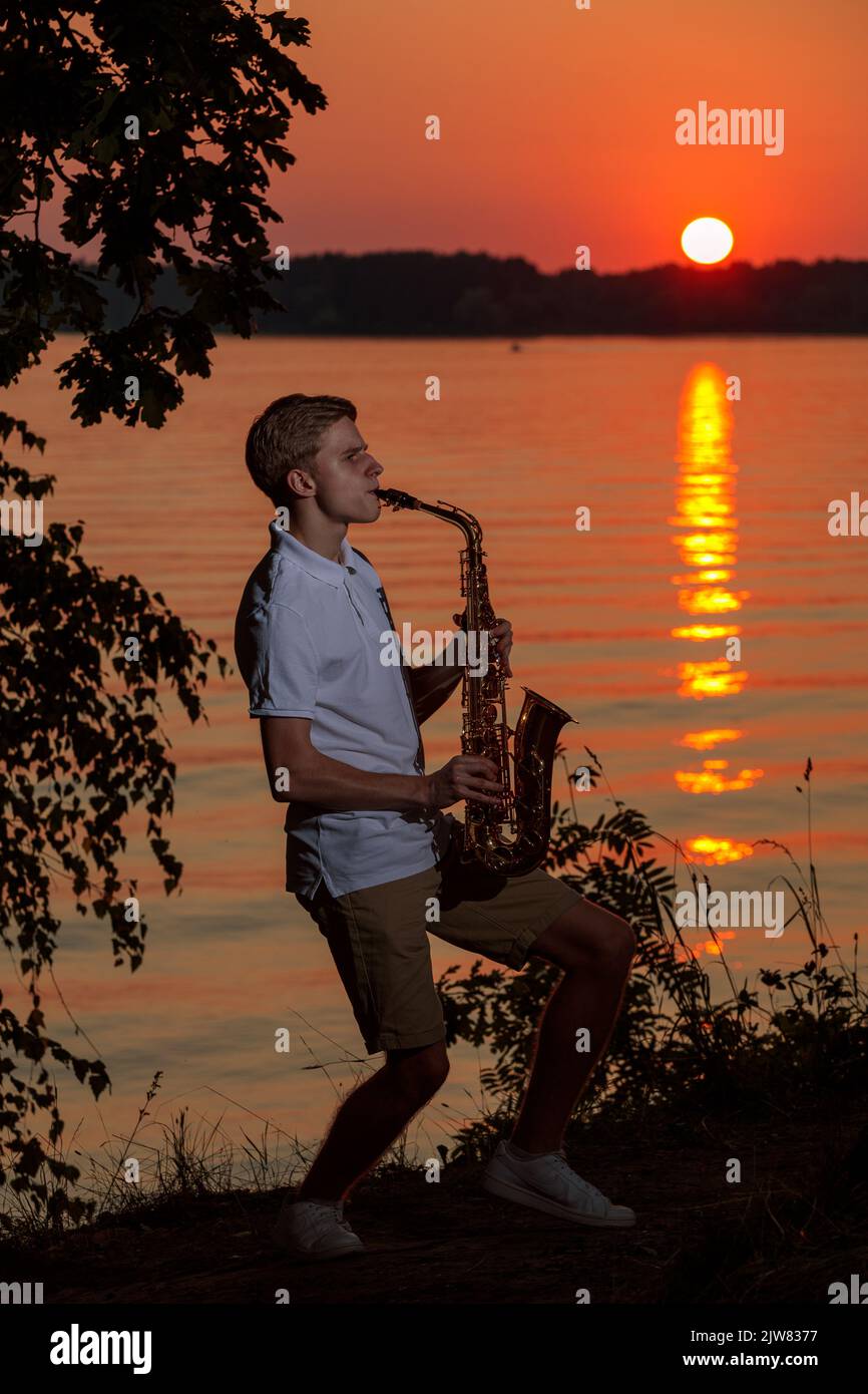 A young guy plays the saxophone in the evening at sunset Stock Photo ...