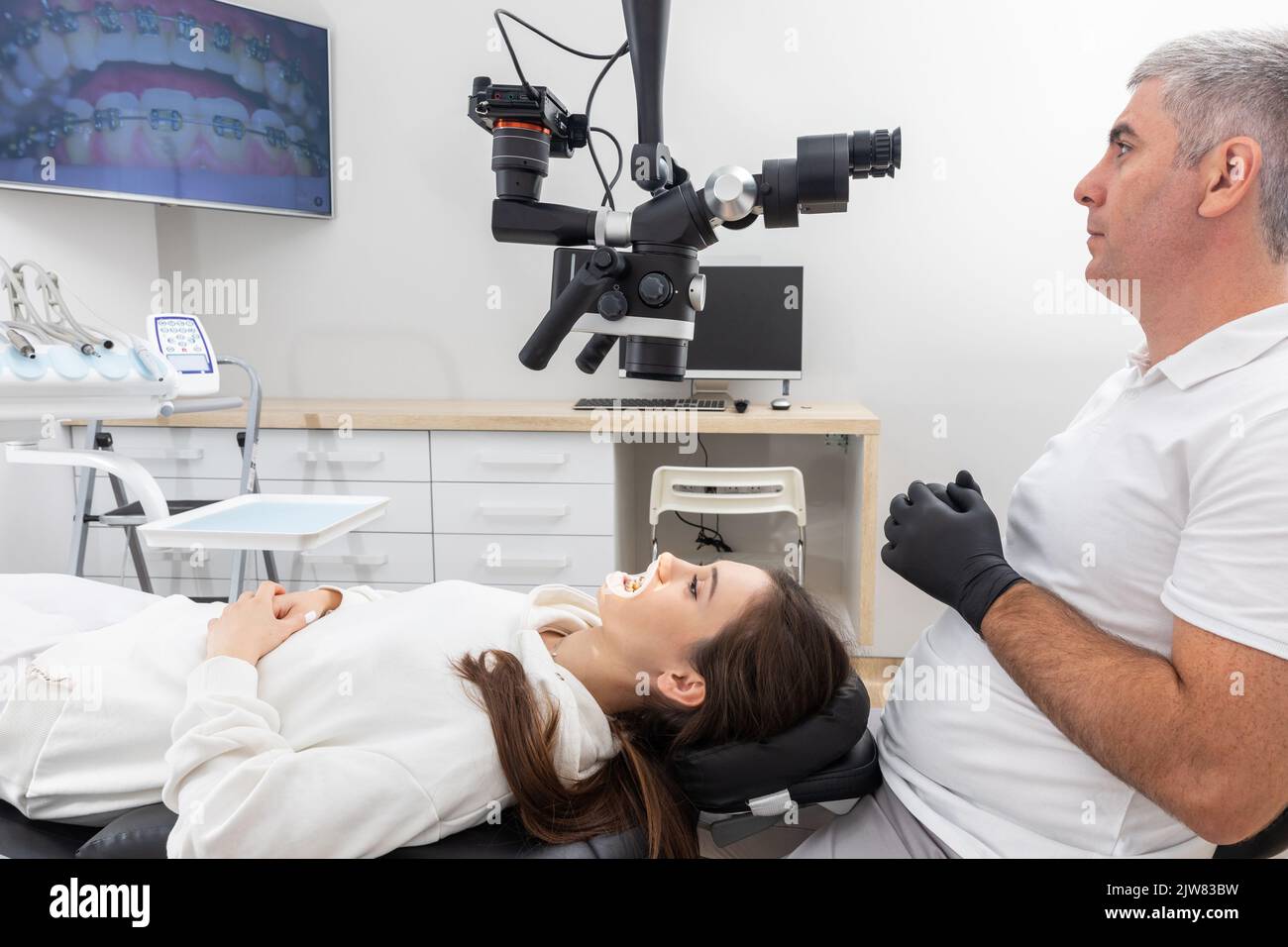 Dentist using dental microscope treating patient with braces in dental ...