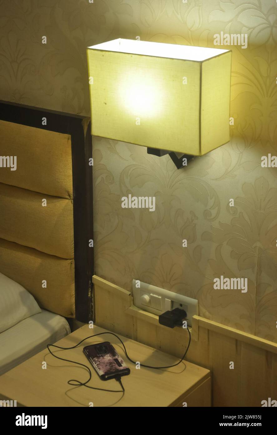Mobile phone on charge on the table near to bed and wall light lamp ...