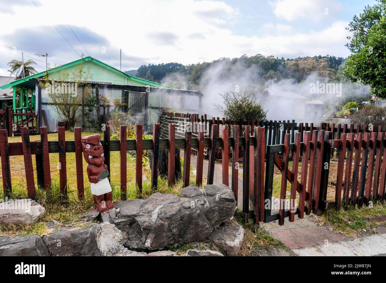 Steam rising from a hot spring in a small garden in front of a Maori ...